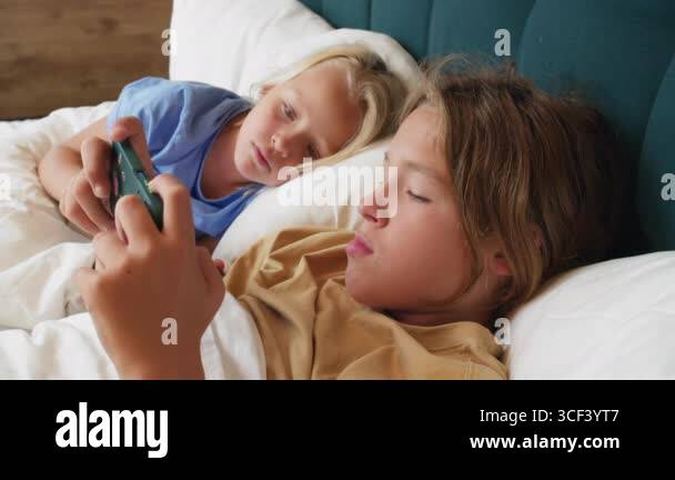 Close up of a child focused on a smartphone screen while another ...