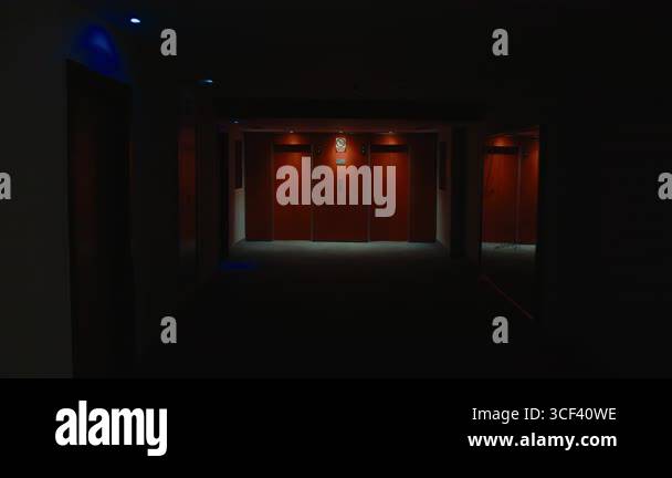 Dark, empty corridor revealing red elevator doors at night, camera ...
