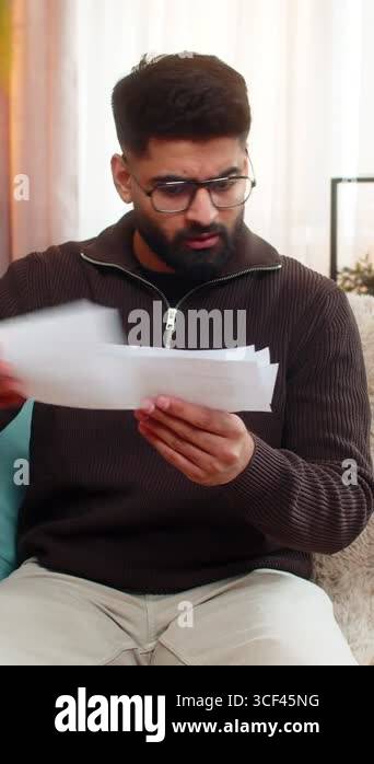 Indian man at home checks bills receipts with tense expression ...
