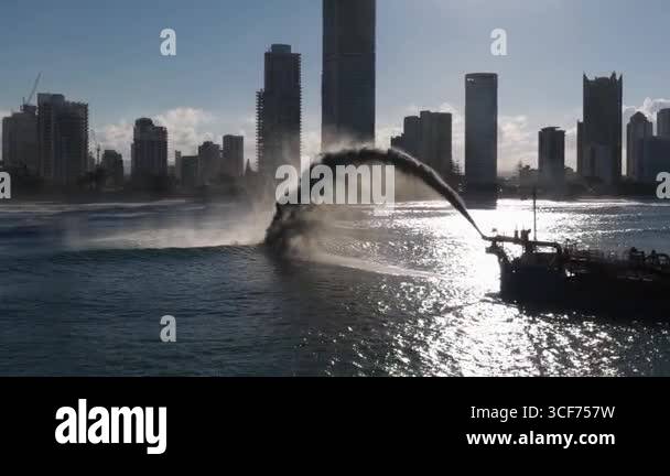 A dredging ship pumps sand to restore a beach, silhouetted against a ...