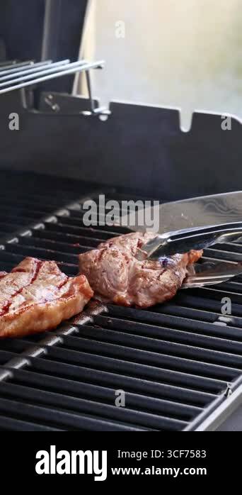 Beef steaks cooking on a grill with tongs flipping them. Outdoor ...