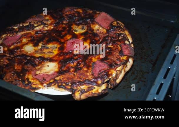 An overcooked pizza sits in the oven with a charred crust and toppings ...