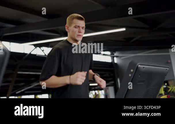 A young, focused man exercises on a treadmill in a modern gym, depicting health and fitness ...