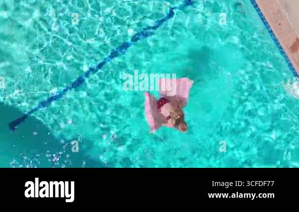 Overhead drone shot of a young girl joyfully jumping off a pink ...