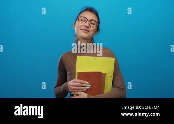 Woman smiling and holding folders against an isolated blue background ...