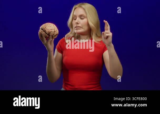 Woman holding brain with crossed fingers poses against blue background ...