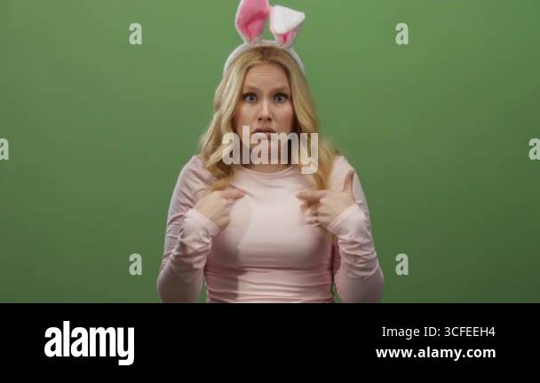 Woman with blonde hair wearing bunny ears and pink shirt gestures ...
