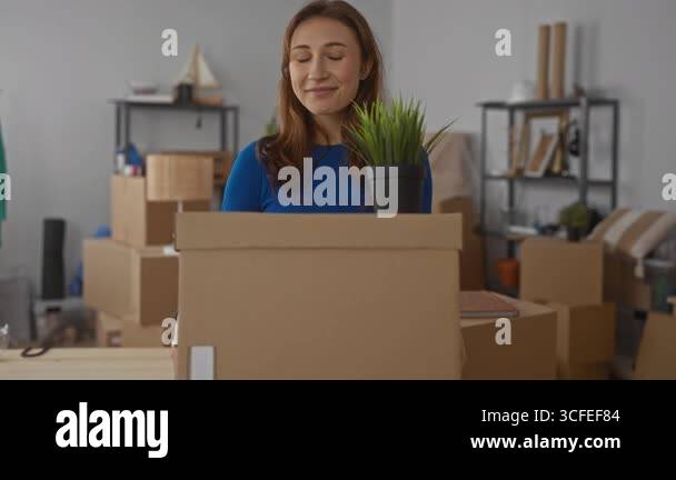 Woman in blue moving boxes in new apartment surrounded by packed items ...