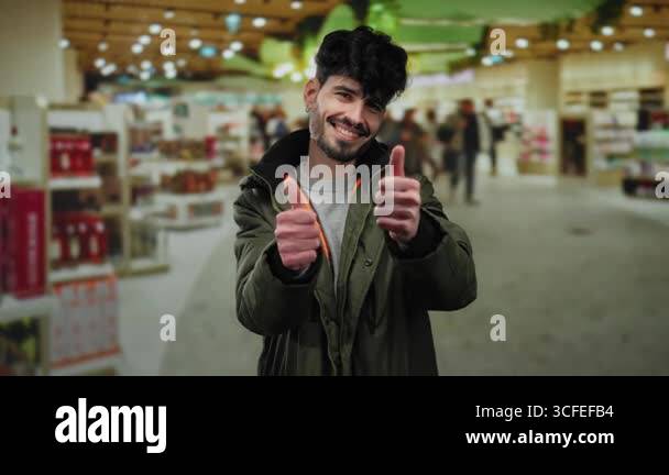 Young man in a mall giving thumbs up while smiling, surrounded by ...