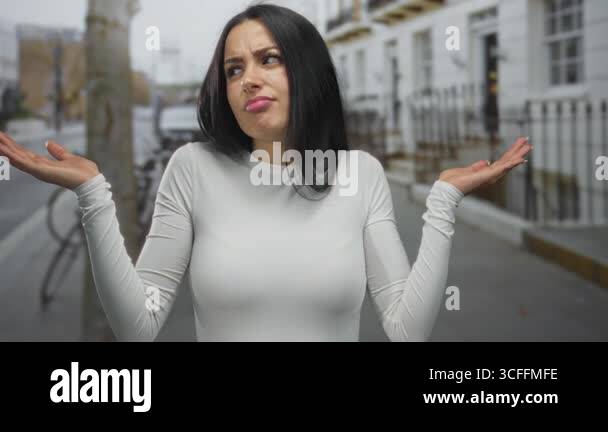 Woman on city street with a puzzled expression, wearing a white shirt ...