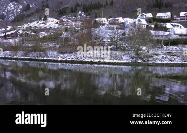 Winter harbor scene with calm fjord water boats and snowy village homes ...