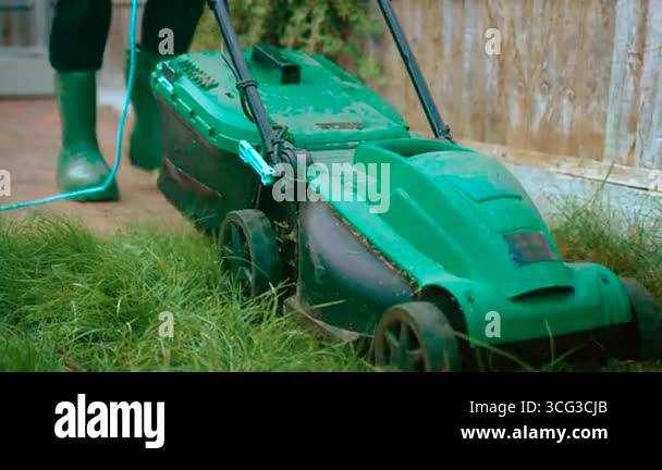 Man mowing grass with electric lawn mower wearing rubber boots. Cutting ...