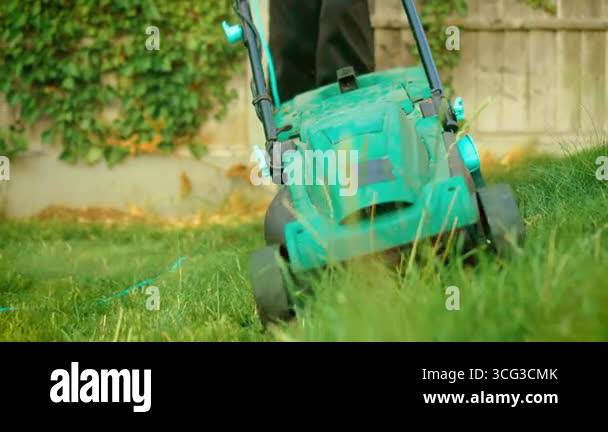 Electric lawn mower cutting grass on awkward slope of backyard lawn ...
