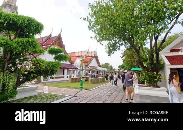 Visitors stroll through Wat Arun, Bangkok, under bright daylight, capturing the temple's ...
