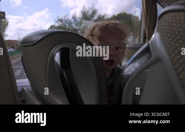 Toddler peeks between bus seats with playful expression, smiling ...