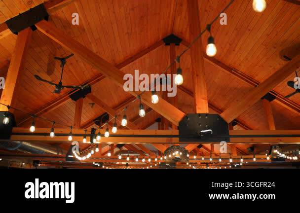 Glowing white bulbs strung across beams in a rustic event hall ...