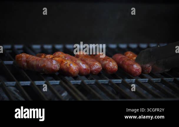 Person is grilling sausages on a gas barbecue grill and closing grill ...