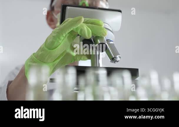 Close up of green gloved hands of a scientist adjusting a microscope in ...