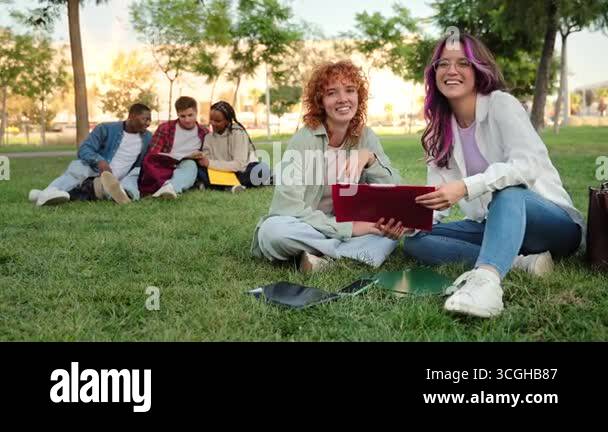 Girl University friend students looking at camera and laughing while studying outdoors with ...