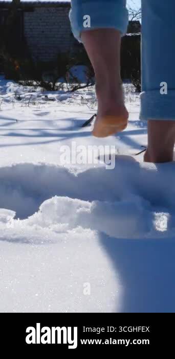 A woman steps barefoot on deep snow. The concept of cold procedures and ...