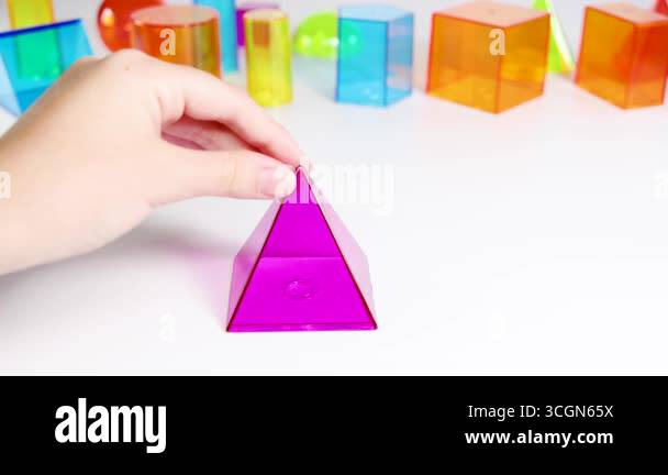 Hands manipulate colorful 3D geometric shapes on a white surface ...