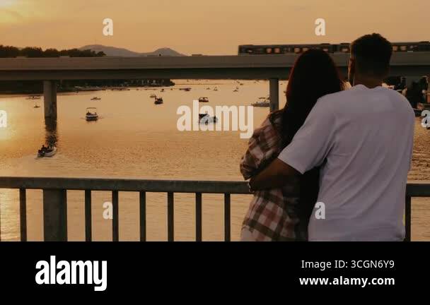 Back view of a young couple standing on a bridge, overlooking a scenic ...