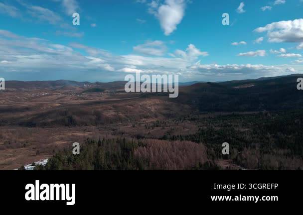 Aerial view of rolling mountains and sparse forest under a sky filled ...