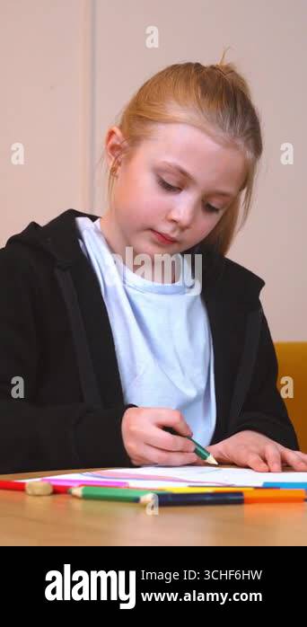 Focused young girl is carefully drawing with colored pencils on a sheet ...
