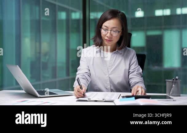 Asian businesswoman making financial calculations using a calculator ...
