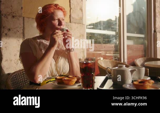 A serene moment of a woman savoring tea and pastries in a sunlit caf ...