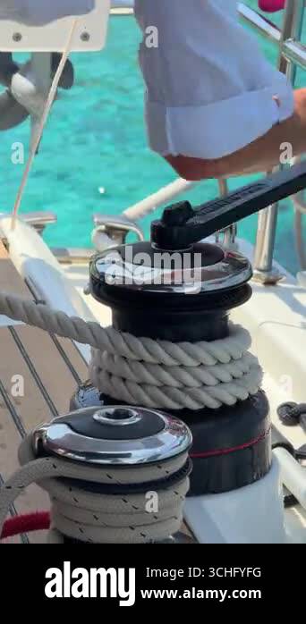 Close-up of hands tightening rope on winch during sail hoisting on ...