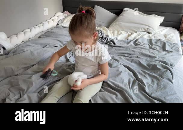 Little girl brushing her plush bunny and braiding its ears while ...