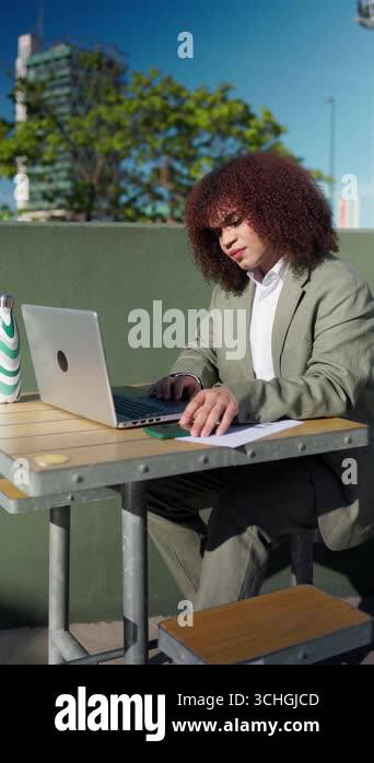 A trans woman in professional attire works outdoors using a laptop and ...