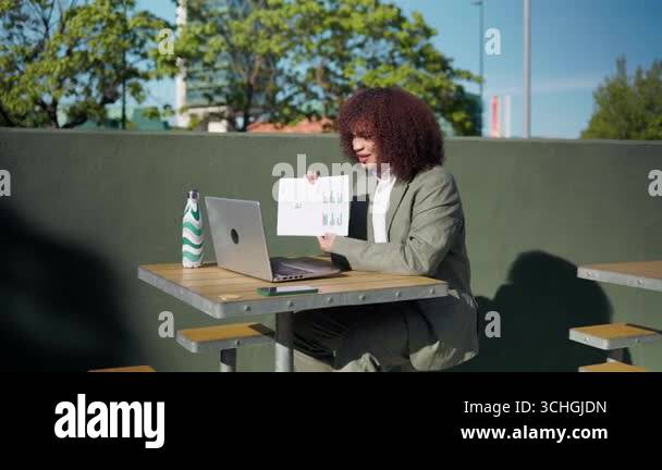 A trans woman in professional attire works outdoors at a picnic table ...