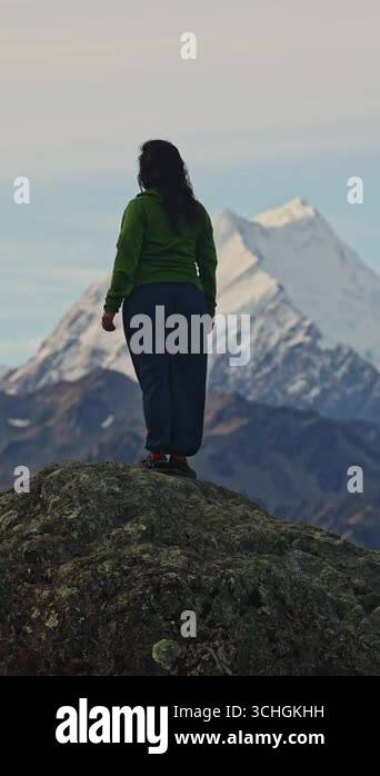 A woman stands on a rock, admiring the majestic Mt. Cook in New Zealand ...