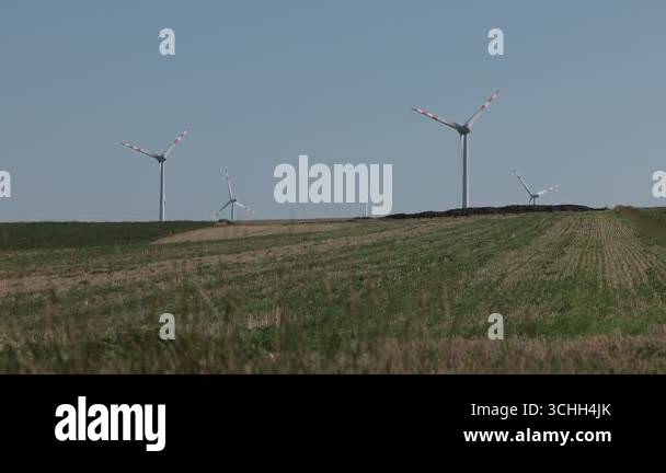 modern wind turbines with red-tipped blades stand tall on a grassy hill ...