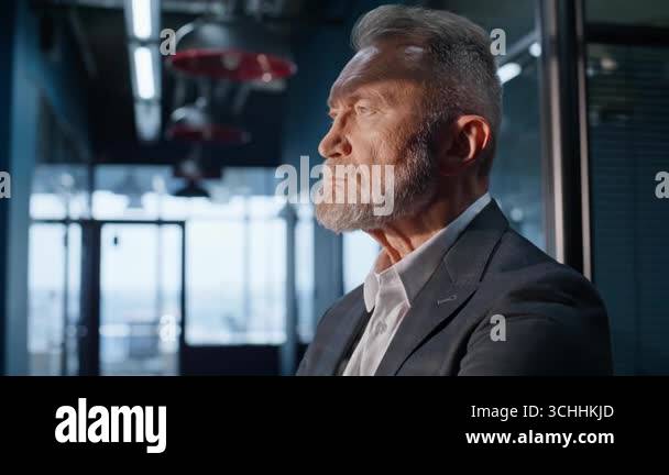 Thoughtful senior businessman standing in modern company hall in ...