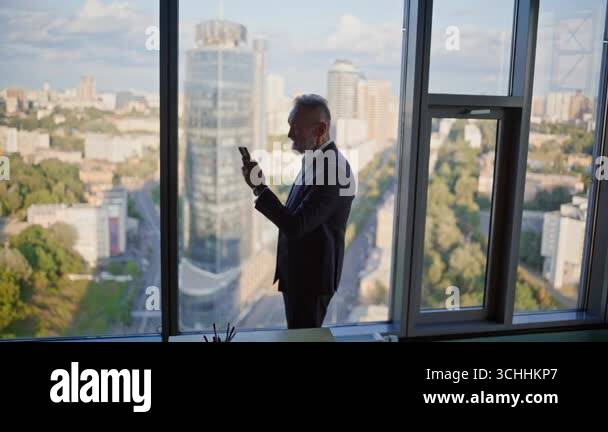 Overjoyed businessman browsing smartphone stand by office panoramic ...