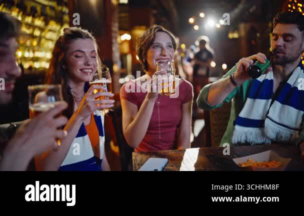 Sport fans clinking beer watching television in dark bar closeup ...