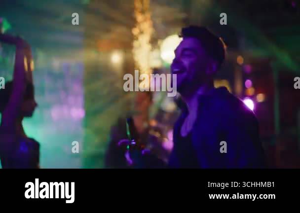 Carefree clubber moving body at dark dancefloor holding beer bottle ...