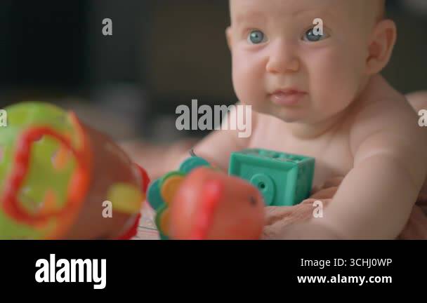 A 3-month-old baby boy lies on the floor and plays with toys, enjoying ...