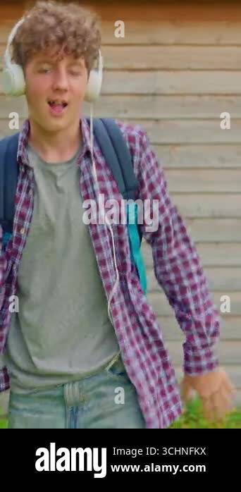 Vertical video. Happy young curly teenager dancing with headphones ...