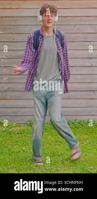 Vertical video. Happy young curly teenager dancing with headphones ...