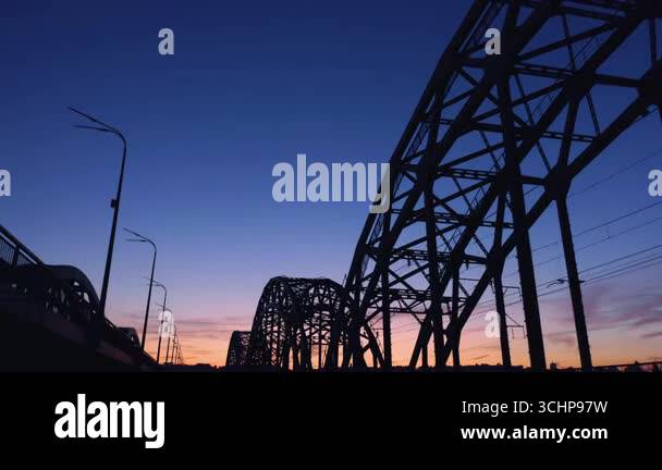 Large steel bridge structure stands against a colorful evening sky. The ...
