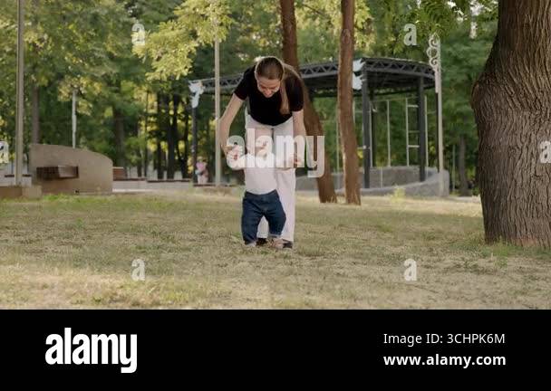 Baby takes first steps while being supported by mother in a lush park ...