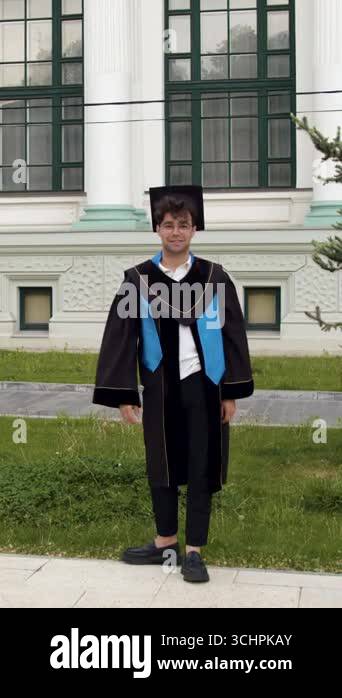 Young graduate student wearing graduation gown and mortarboard stands ...