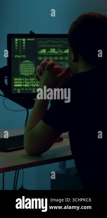 Male software developer is analyzing code on dual monitors in a dark environment, showcasing the ...