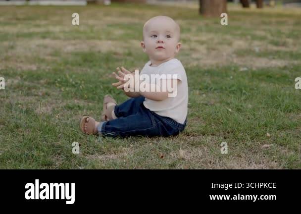 Child seated on grass, enthusiastically clapping hands, expressing joy ...