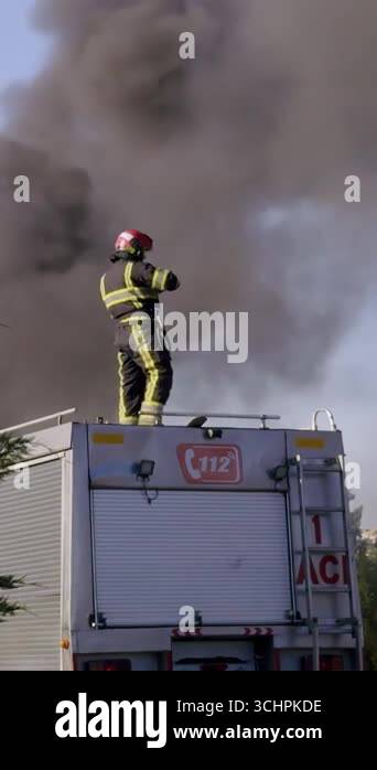 Firefighter in full gear is positioned on fire truck, combating intense ...
