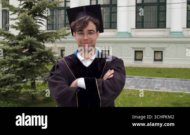 Portrait of an excited graduate boy in graduation gown and cap smiles ...